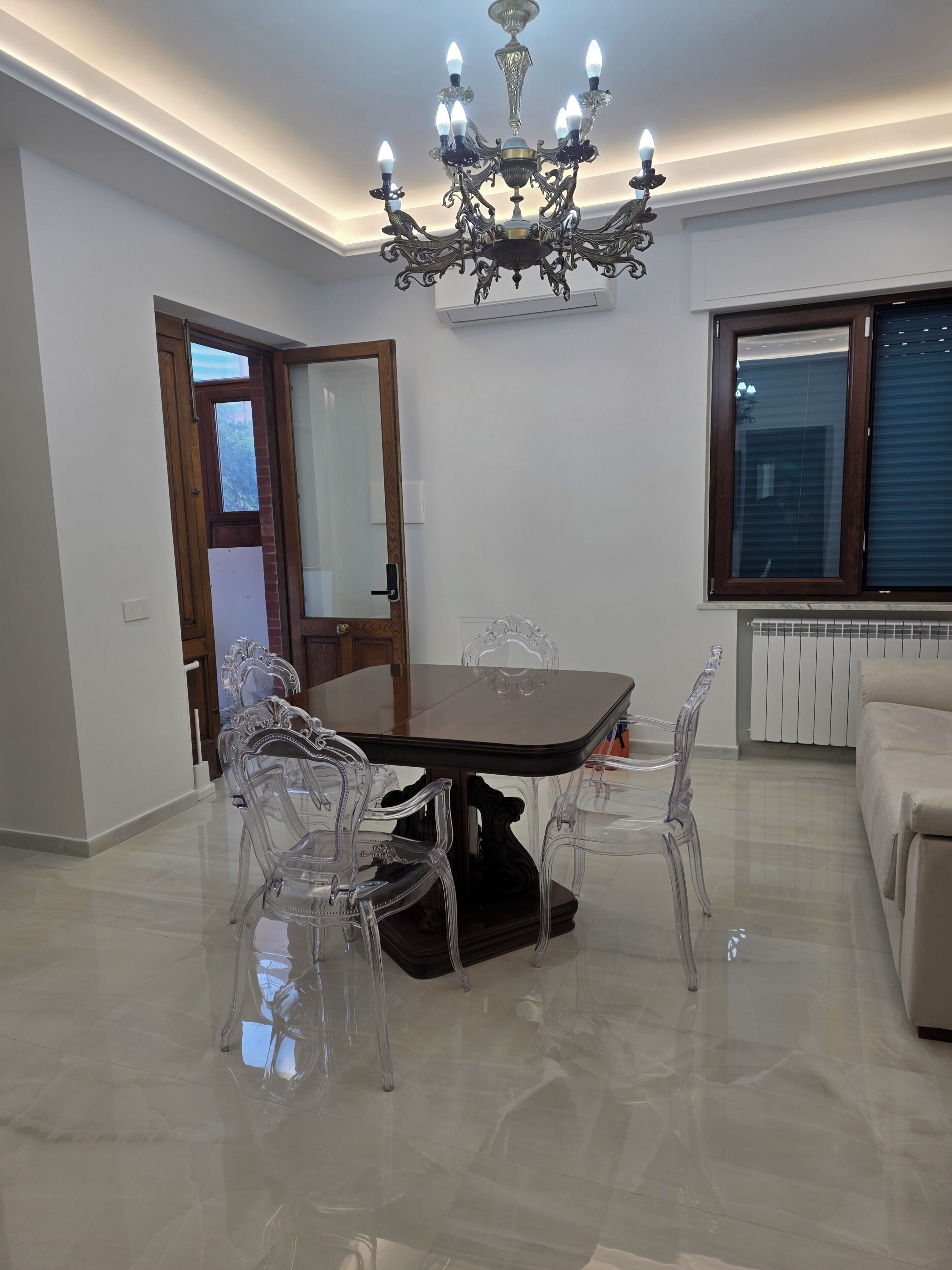 Uma sala de jantar com um candelabro, uma mesa e cadeiras transparentes.