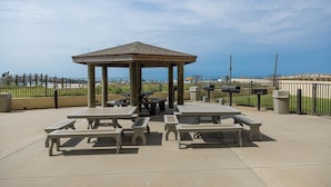 Uma área de pátio ao ar livre com mesas de piquenique e um gazebo, com vista para a praia.