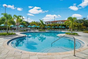 Uma piscina com design curvo, rodeada por espreguiçadeiras e guarda-sóis, com um edifício ao fundo.