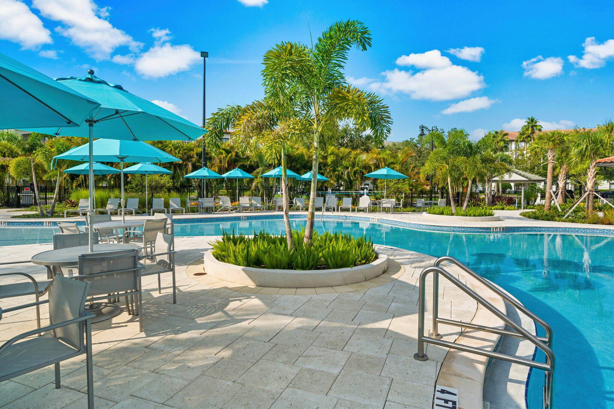 Uma área de piscina com espreguiçadeiras, guarda-sóis e um pequeno jardim.