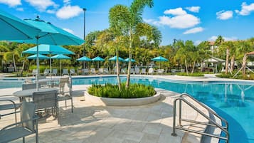 Uma área de piscina com espreguiçadeiras, guarda-sóis e um pequeno jardim.