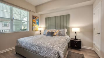 Quarto com cama, duas mesas de cabeceira, um criado-mudo, janela com persianas e um quadro na parede.