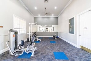 Academia com equipamentos de exercício, espelho e carpete azul.