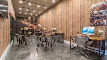 Interior de restaurante com paredes de madeira, várias mesas e cadeiras, uma mesa de escritório e uma televisão.
