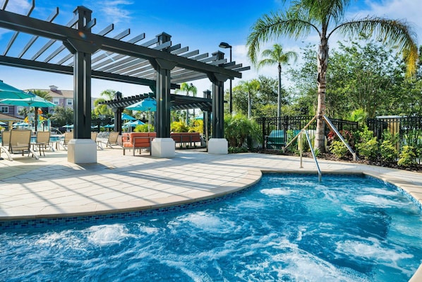 Uma área de piscina com hidromassagem, espreguiçadeiras e guarda-sóis.