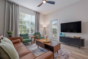 Uma sala de estar moderna com um sofá, cadeiras, uma mesa de centro, uma televisão e um ventilador de teto.