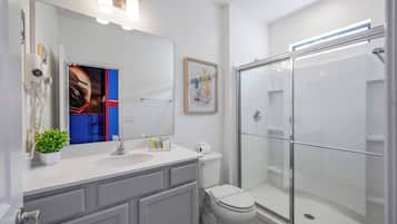 Uma casa de banho moderna com um espelho grande, lavatório, sanita e cabine de duche com parede de vidro.