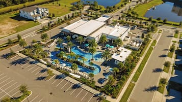 Vista aérea de um hotel com piscina, estacionamento e vegetação ao redor.