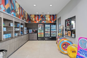 Uma loja bem iluminada com prateleiras repletas de diversos produtos, balcões refrigerados e coloridos flutuadores infláveis.