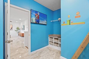 Um corredor com parede azul, um quadro com a imagem de Mario e uma prateleira com objetos temáticos de Mario.
