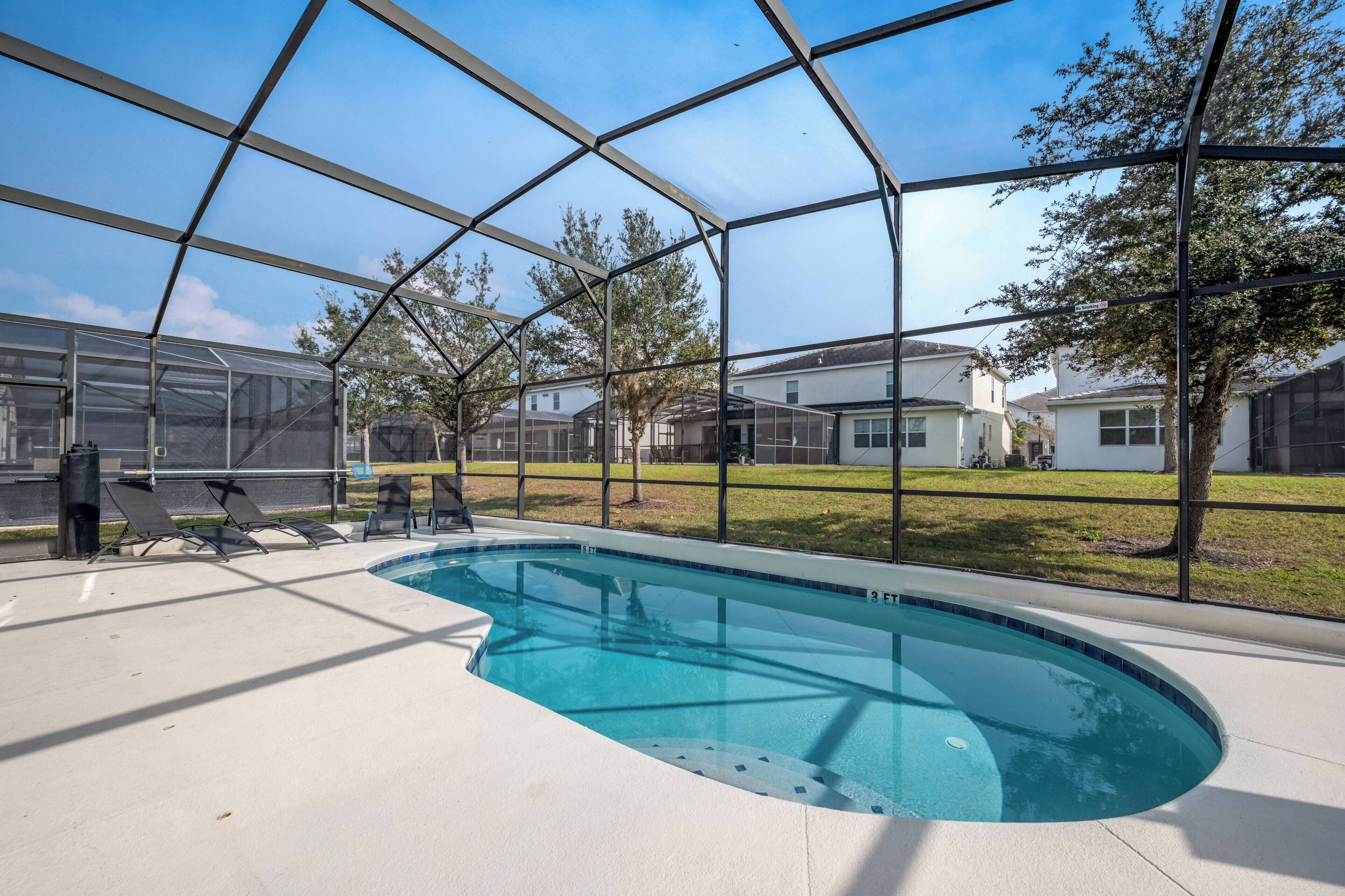 Piscina com estrutura de vidro, cercada por grade metálica e vista livre para o bairro.