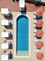Piscina com espreguiçadeiras e guarda-sóis, rodeada por um deck revestido de azulejos.