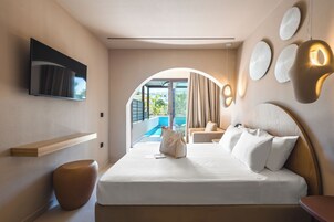Quarto de hotel moderno com cama, televisão, mesa pequena, sofá e vista para uma piscina.