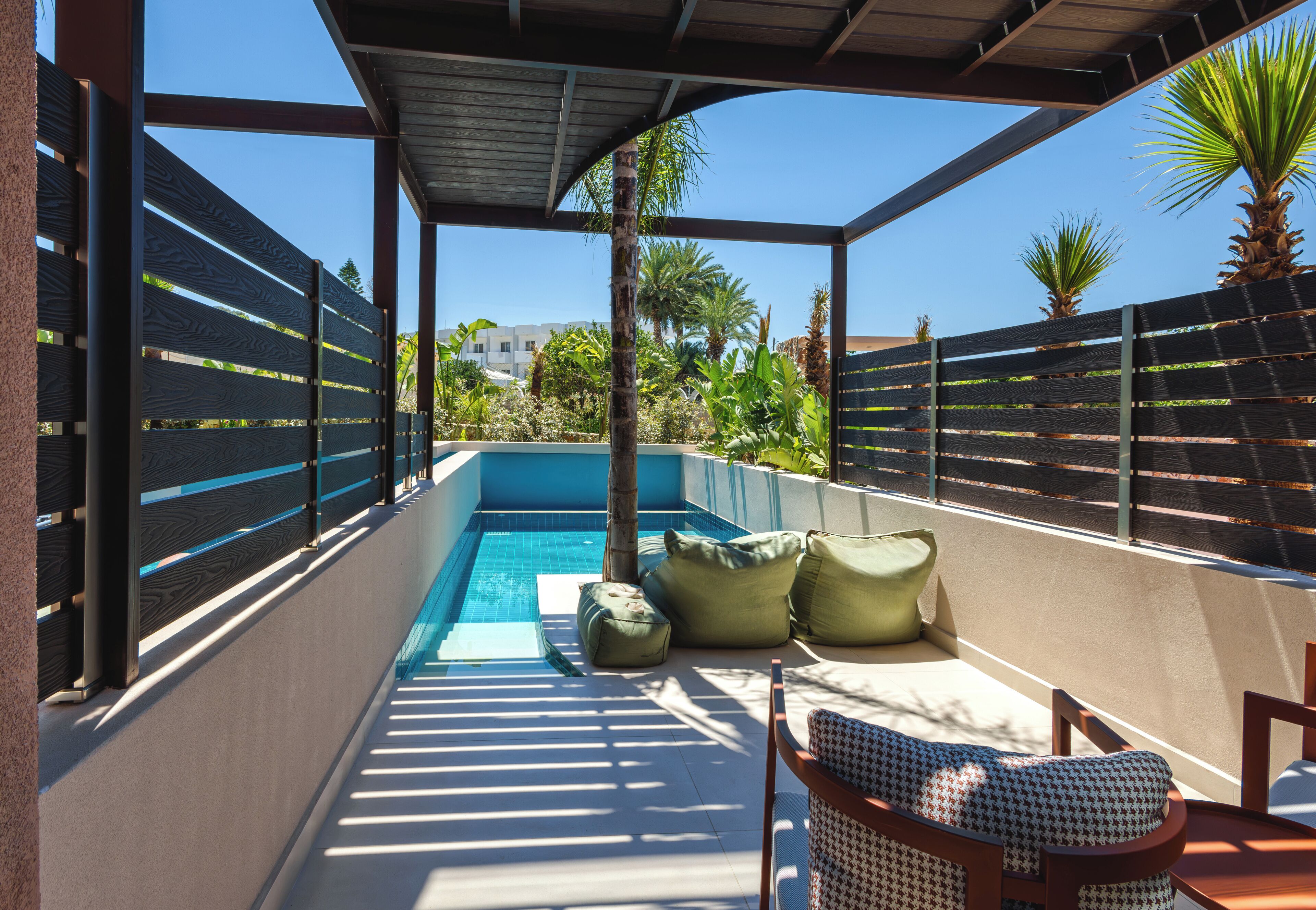 Uma área de piscina no terraço com vista clara do céu, cercada por um muro de madeira, e com espaço para sentar com almofadas.