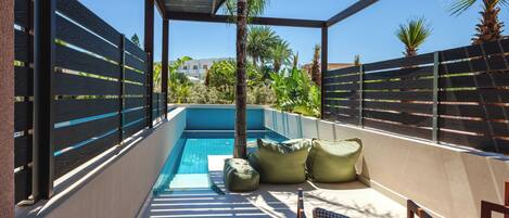 Uma área de piscina no terraço com vista clara do céu, cercada por um muro de madeira, e com espaço para sentar com almofadas.