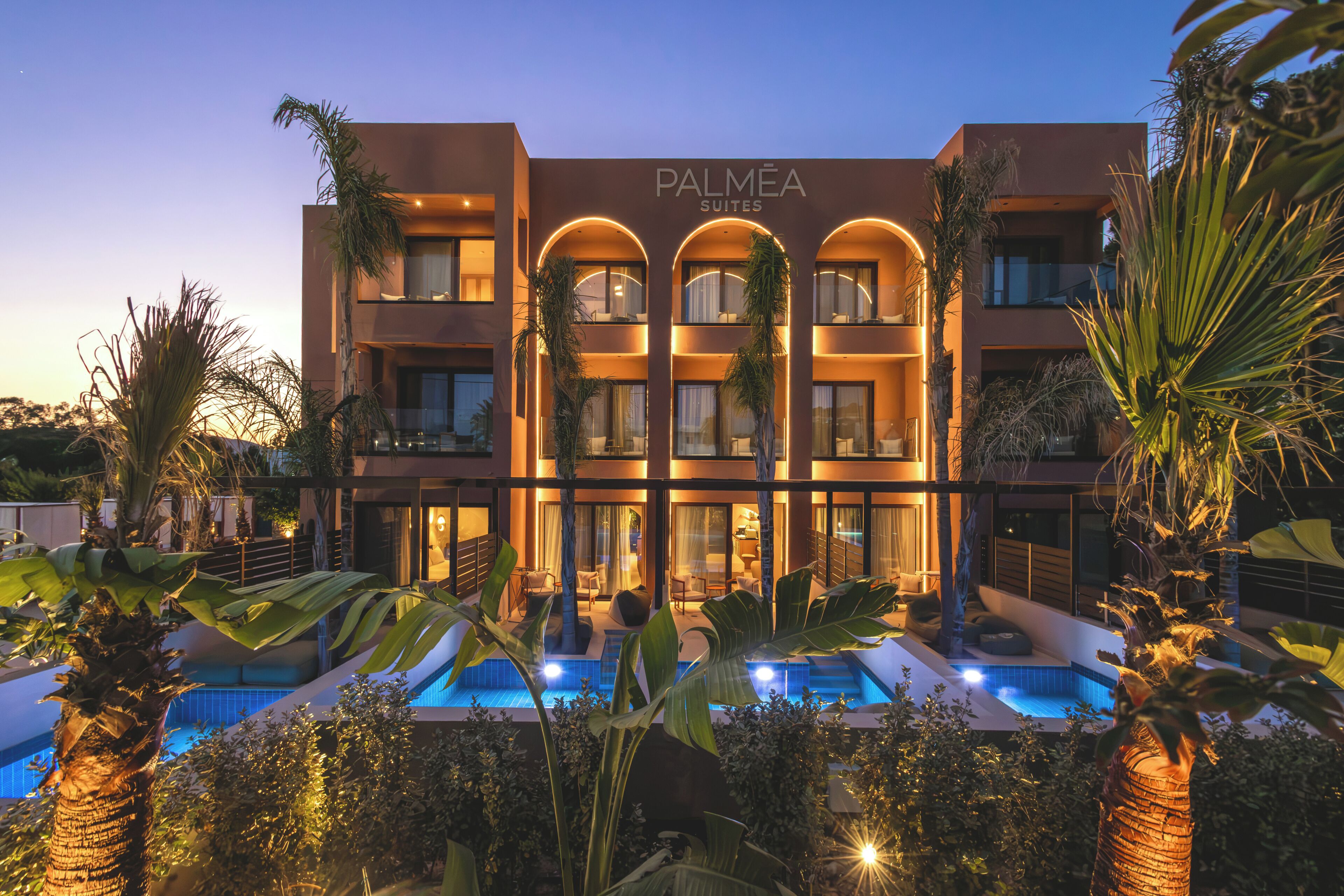 Um hotel moderno com piscina, várias varandas e exuberante vegetação tropical.