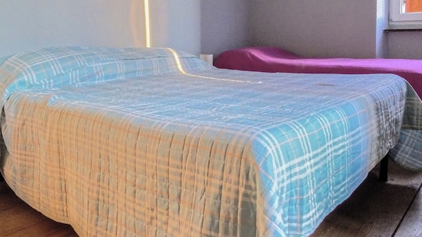 Um quarto com duas camas, uma com colcha xadrez azul e branca e a outra com colcha roxa.