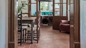 Uma sala de jantar com mesa e cadeiras de madeira, uma lareira e vista para a cozinha.