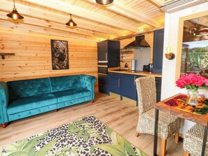 Um quarto acolhedor com um sofá verde-água, uma mesa de jantar com um vaso de flores e uma cozinha com armários de madeira e um lustre.