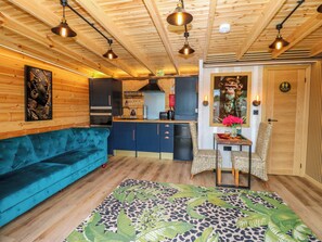 Interior acolhedor de uma cabana, com um sofá azul, área de cozinha e um espaço de jantar com cadeiras de vime.