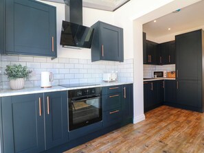 Cozinha moderna com armários escuros, forno embutido, micro-ondas e televisão de tela plana.
