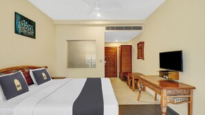 Quarto de hotel com cama, escrivaninha, televisão e um quadro na parede.