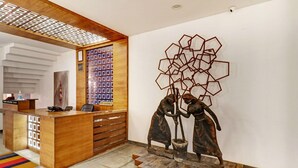 Uma área de recepção com uma mesa de madeira, um telefone e uma escultura na parede de duas figuras.