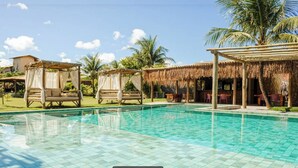 Uma área de piscina com espreguiçadeiras e uma estrutura com telhado de palha.
