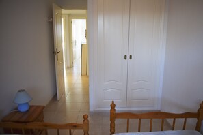 Um quarto com uma cama de madeira, uma mesa de cabeceira com abajur e um guarda-roupa branco.