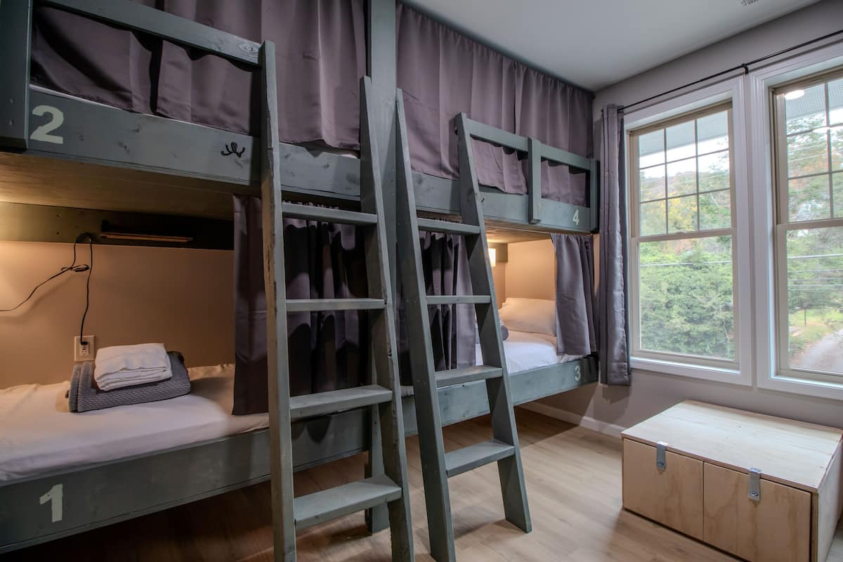 Quarto com beliche, um pequeno armário de madeira e janela com vista para árvores.