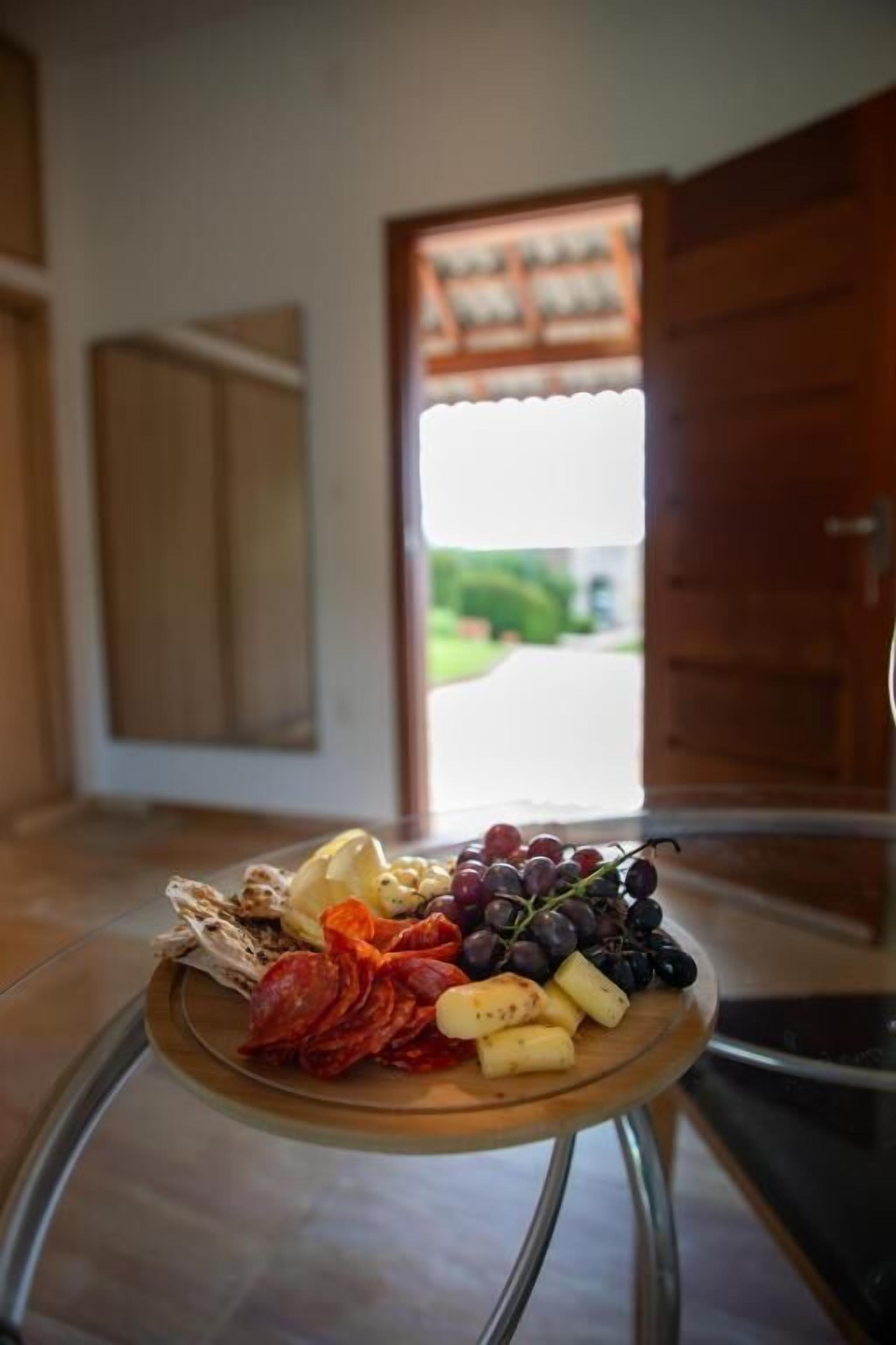 Uma mesa redonda com diversos queijos, uvas e charcutaria.