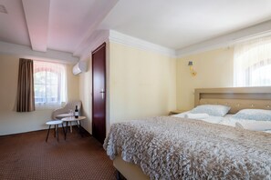 Quarto de hotel com cama, cadeira, mesa pequena e janela com cortinas.