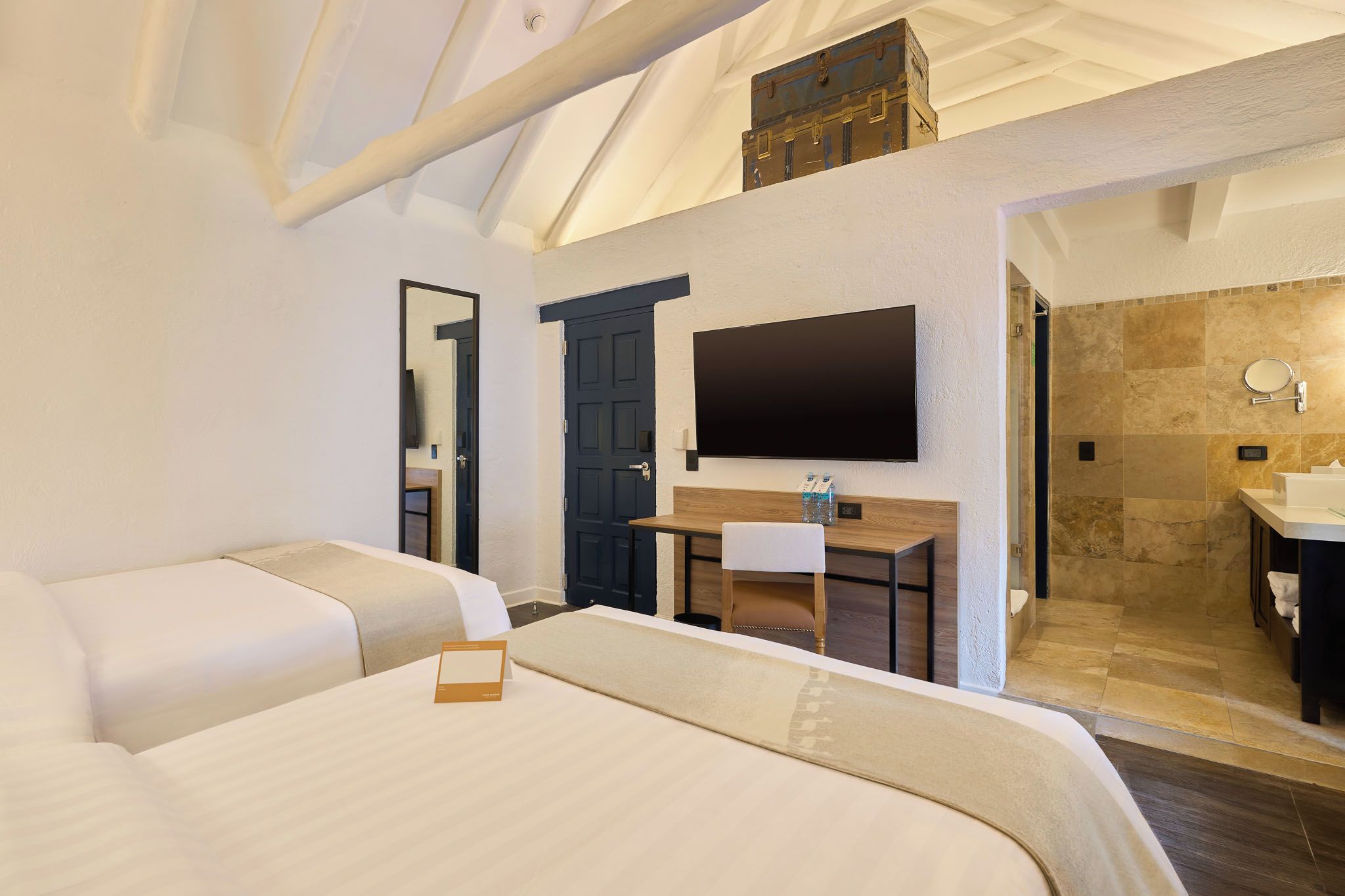 Quarto de hotel com cama, escrivaninha, televisão e banheiro.