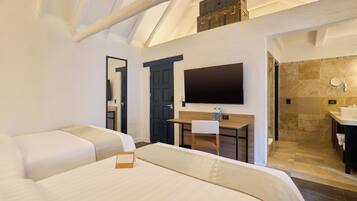 Quarto de hotel com cama, escrivaninha, televisão e banheiro.