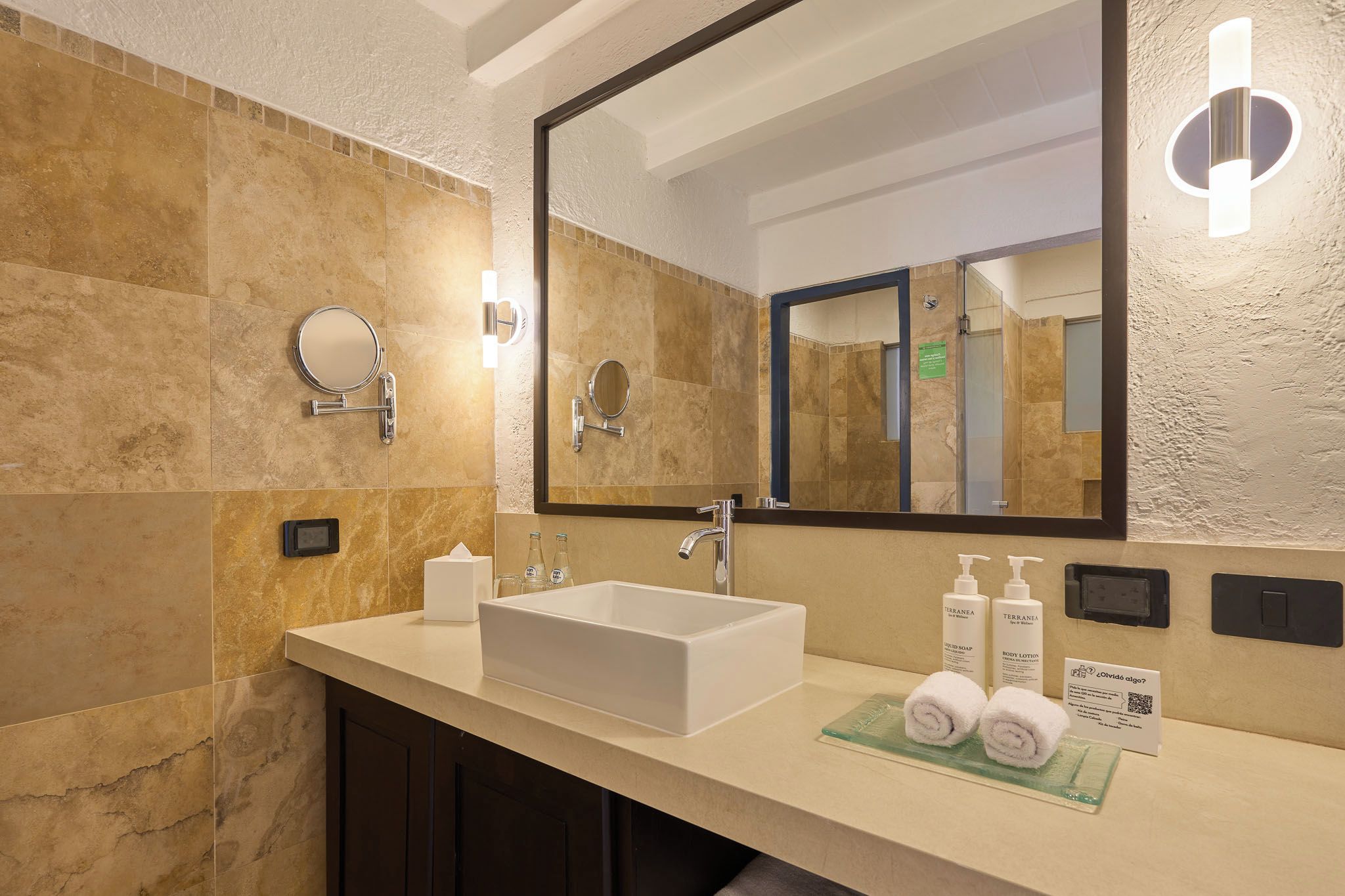 Casa de banho com lavatório branco, dois espelhos e artigos de higiene no balcão.