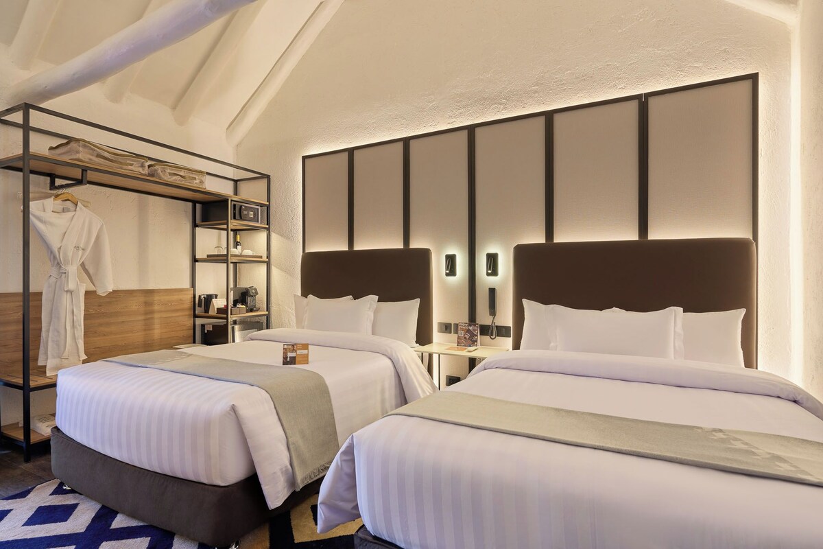 Quarto de hotel com duas camas, porta-robes e minibar.