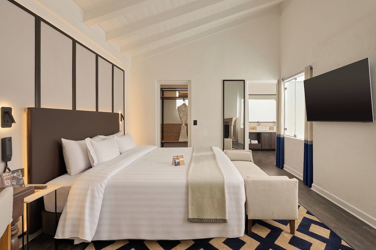 Quarto de hotel com cama grande, mesas de cabeceira, televisão de tela plana, banheiro com espelho e closet espaçoso.