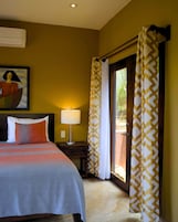 Quarto de hotel com cama, mesa de cabeceira, abajur, quadro na parede e janela com cortinas.