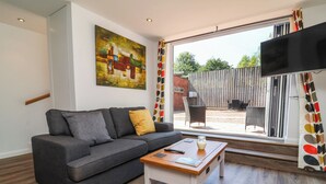 Uma sala de estar com um sofá cinzento, uma mesa de centro, um quadro na parede e uma TV fixada na parede.