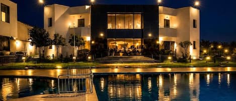 Hotel moderno com piscina, área externa coberta e entrada bem iluminada.