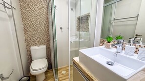Uma casa de banho moderna com cabine de duche em vidro, sanita e lavatório com artigos de higiene pessoal.