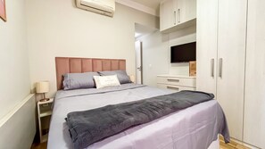 Quarto com cama, mesas de cabeceira, televisão e guarda-roupa.