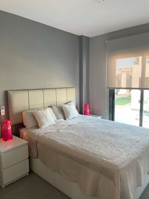 Quarto moderno com uma cama grande, duas mesas de cabeceira e uma janela com vista para o exterior.