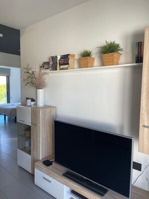 Uma sala de estar moderna com televisão de tela plana, estantes de madeira com livros e plantas, e um design minimalista.