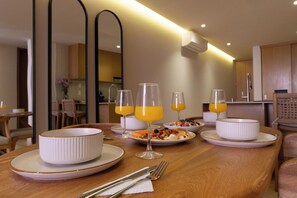 Uma mesa de jantar posta com pratos, tigelas, copos e talheres, com uma cozinha ao fundo.