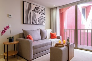 Uma sala de estar moderna com um sofá cinzento, duas almofadas vermelhas, uma mesa lateral com uma planta em vaso e um grande quadro abstrato na parede.