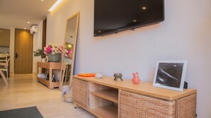Uma sala de estar moderna com uma televisão de tela plana na parede, uma mesa de console de madeira com objetos decorativos, um espelho e uma porta que dá para outro cômodo.