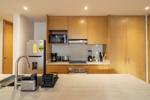 Cozinha moderna com armários de madeira, micro-ondas embutido, cafeteira e dispensador de água.