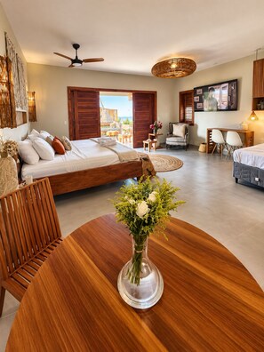 Um quarto amplo com cama, mesa de jantar com cadeiras, ventilador de teto e vista para o exterior.