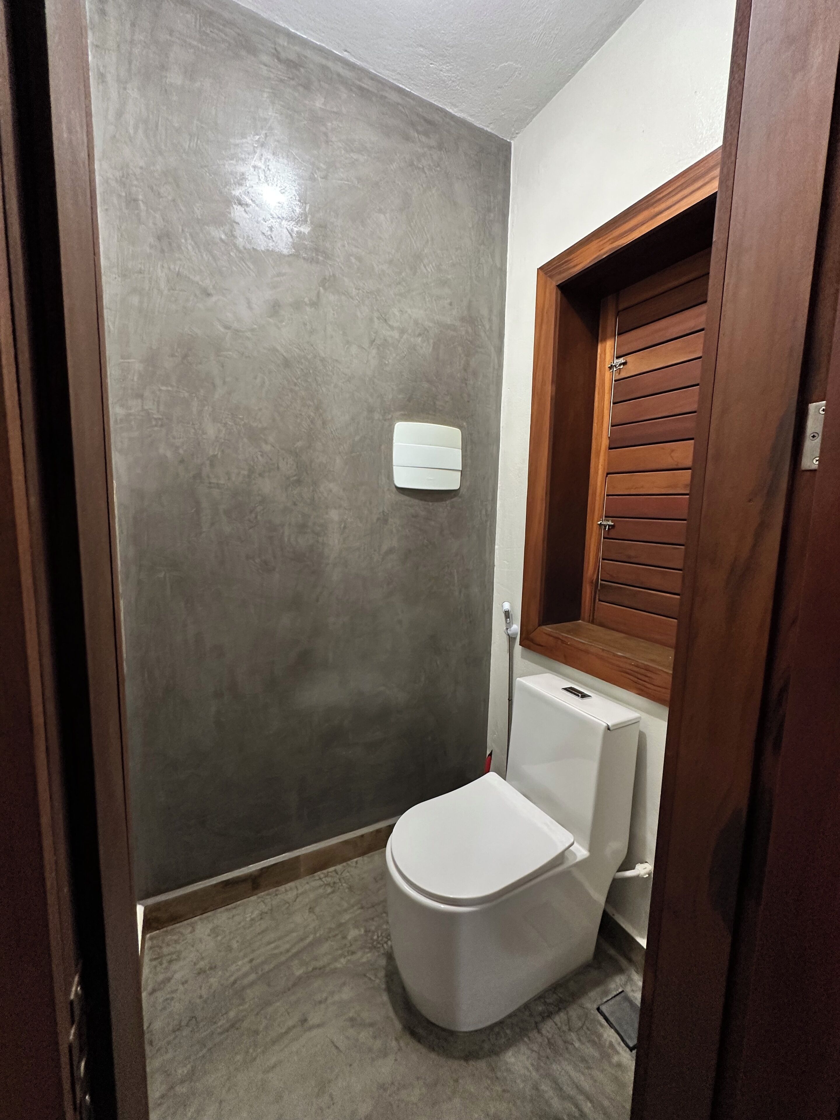Casa de banho com sanita, chuveiro e janela com estores.